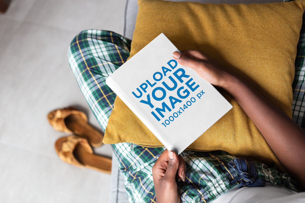 Placeit - Mockup of a Book Held by a Woman's Hands on a Couch
