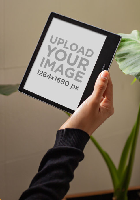 Placeit - Mockup of a Woman's Hand Holding a Kindle Oasis by a House Plant